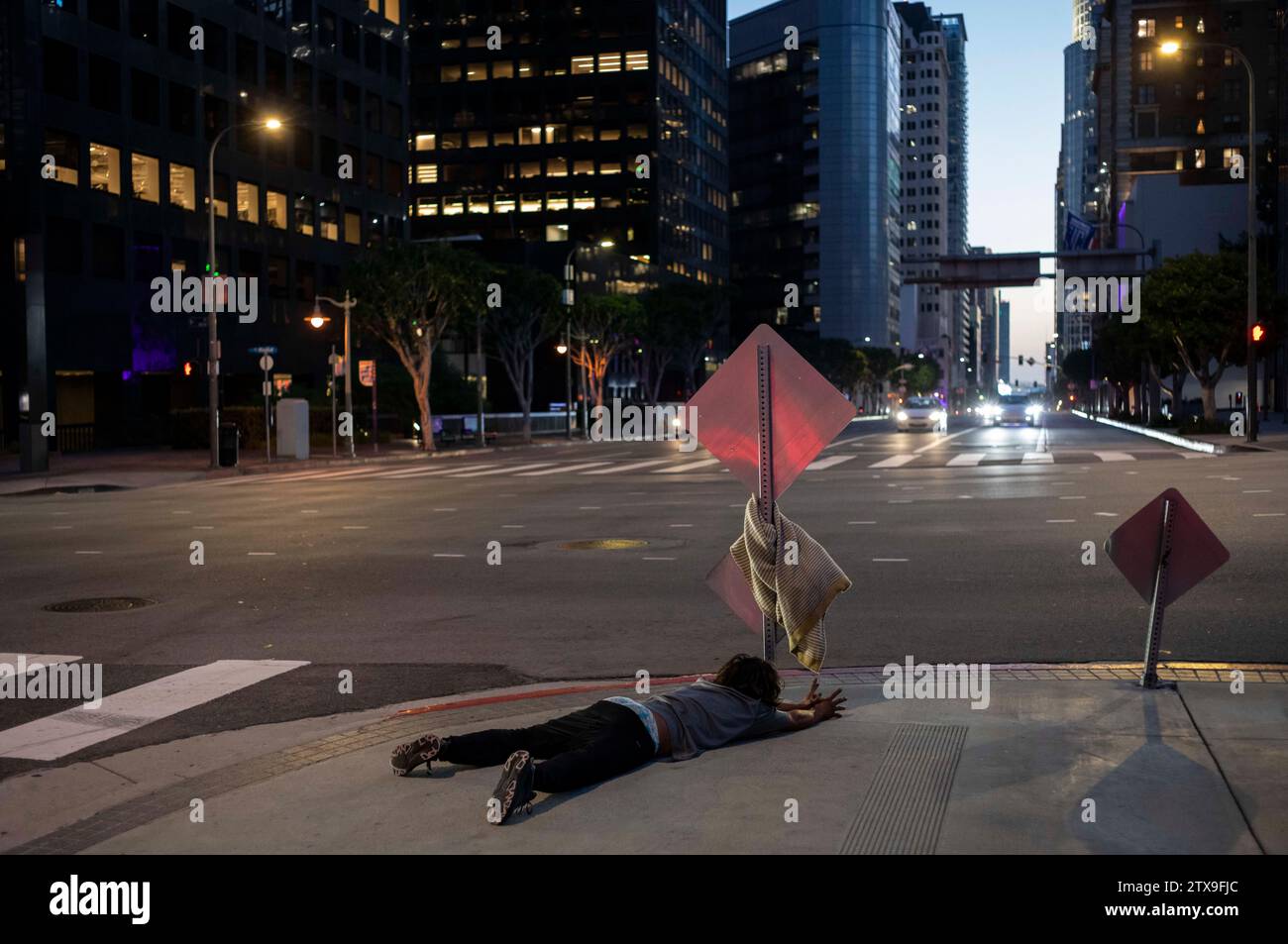 A homeless man screams and extends his arms while lying on a sidewalk ...