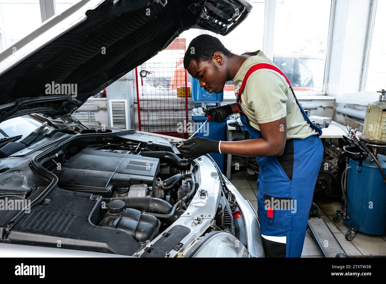 Young African man working under the hood of car fixing engine in auto ...