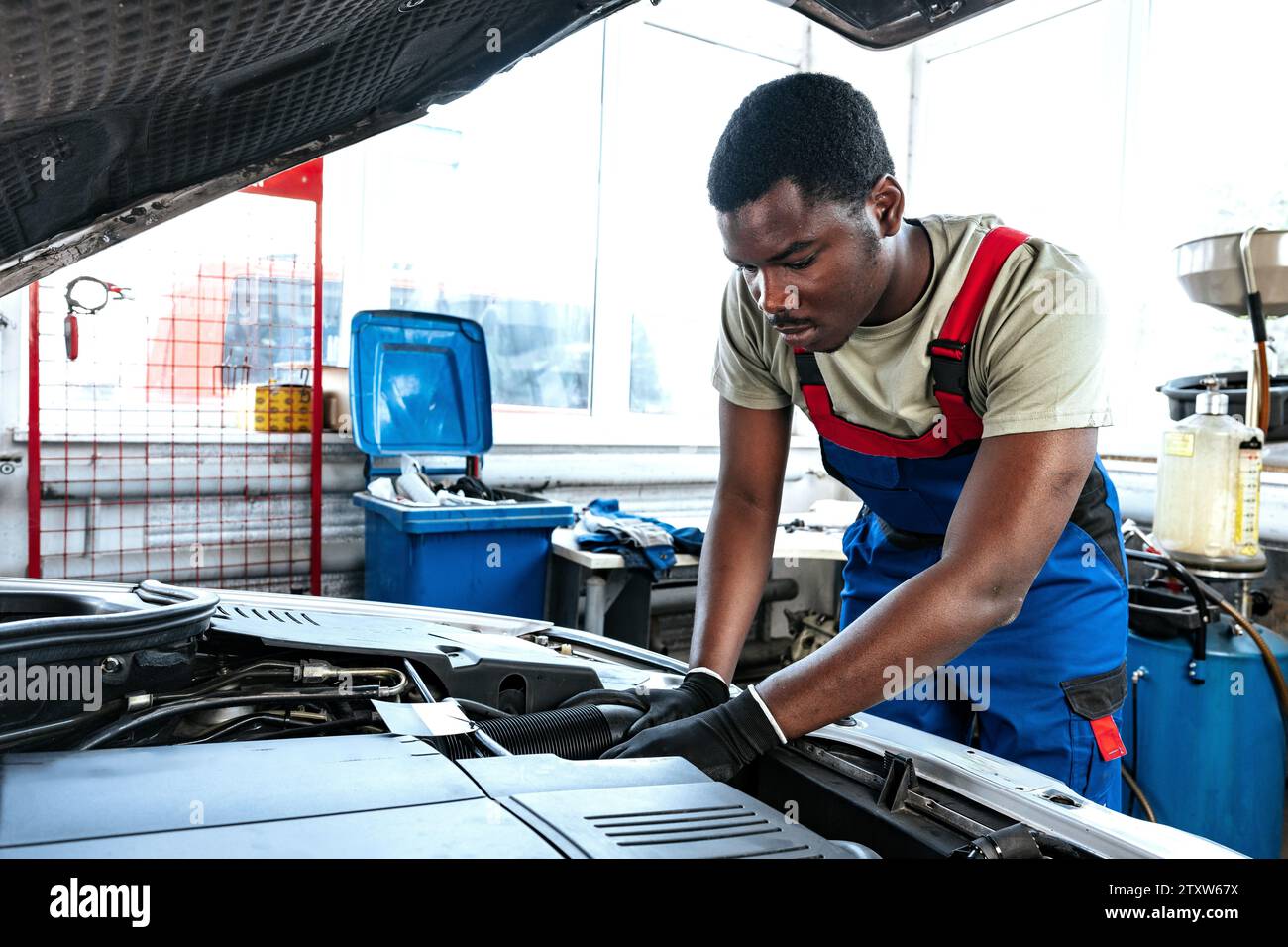 Young African man working under the hood of car fixing engine in auto ...