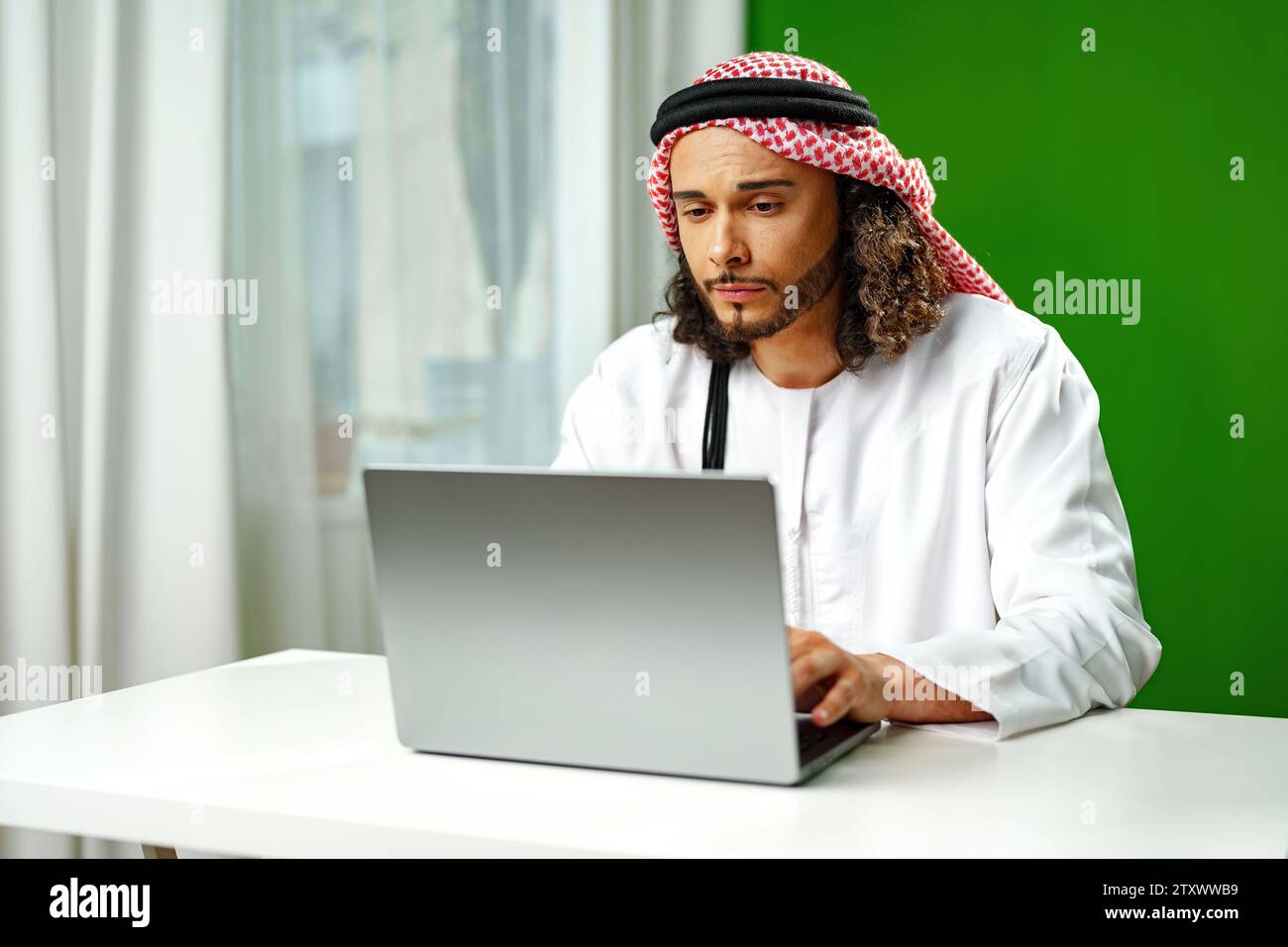 Young Arab man in traditional dress thobe working on computer in office ...