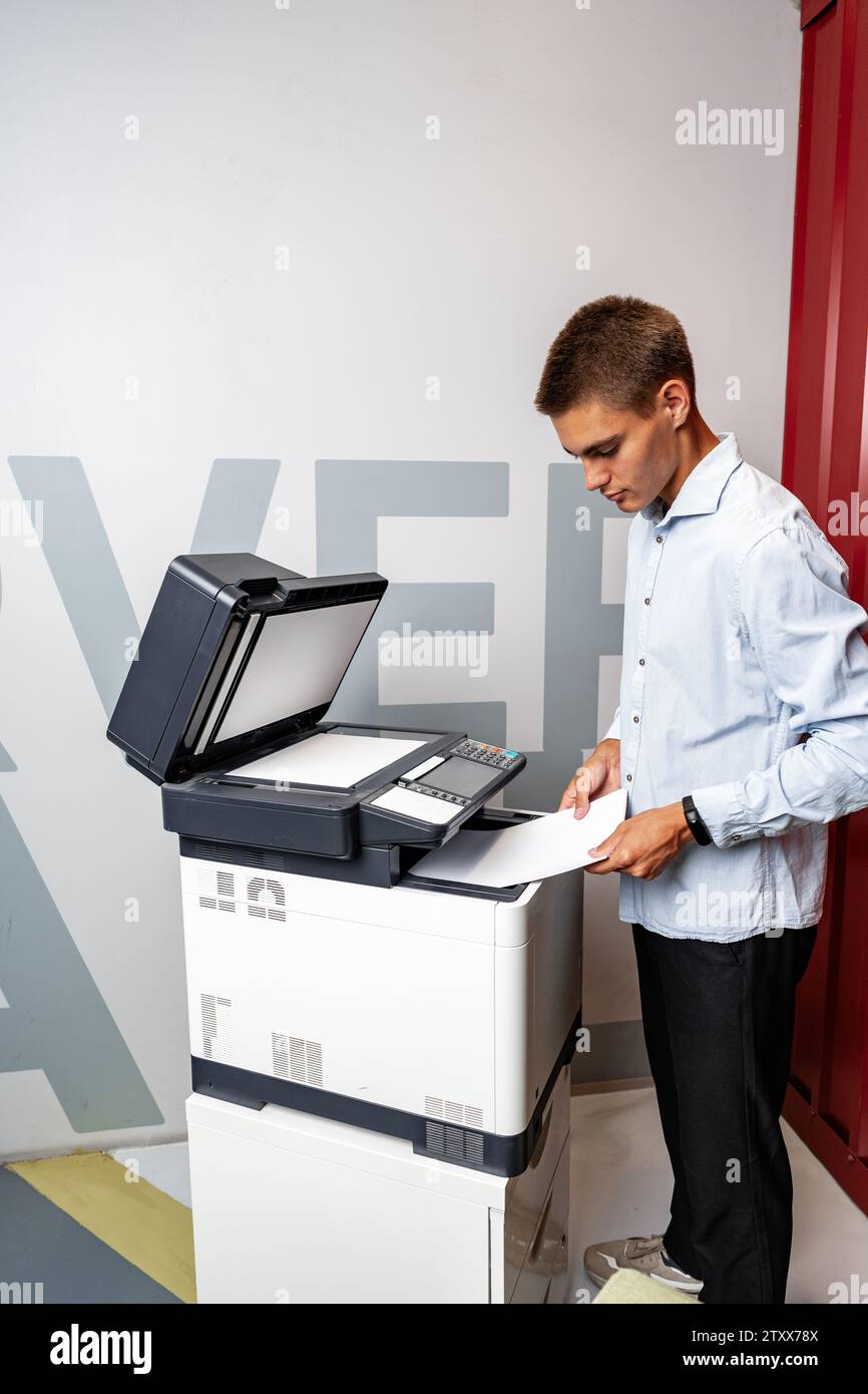 Positive young man using printer in the modern office Stock Photo - Alamy