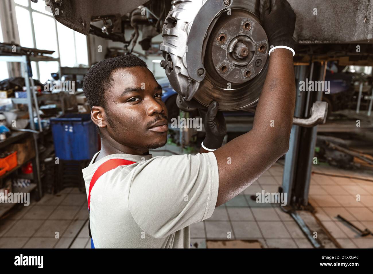 African male auto-mechanic repairing car brakes under the car in auto ...