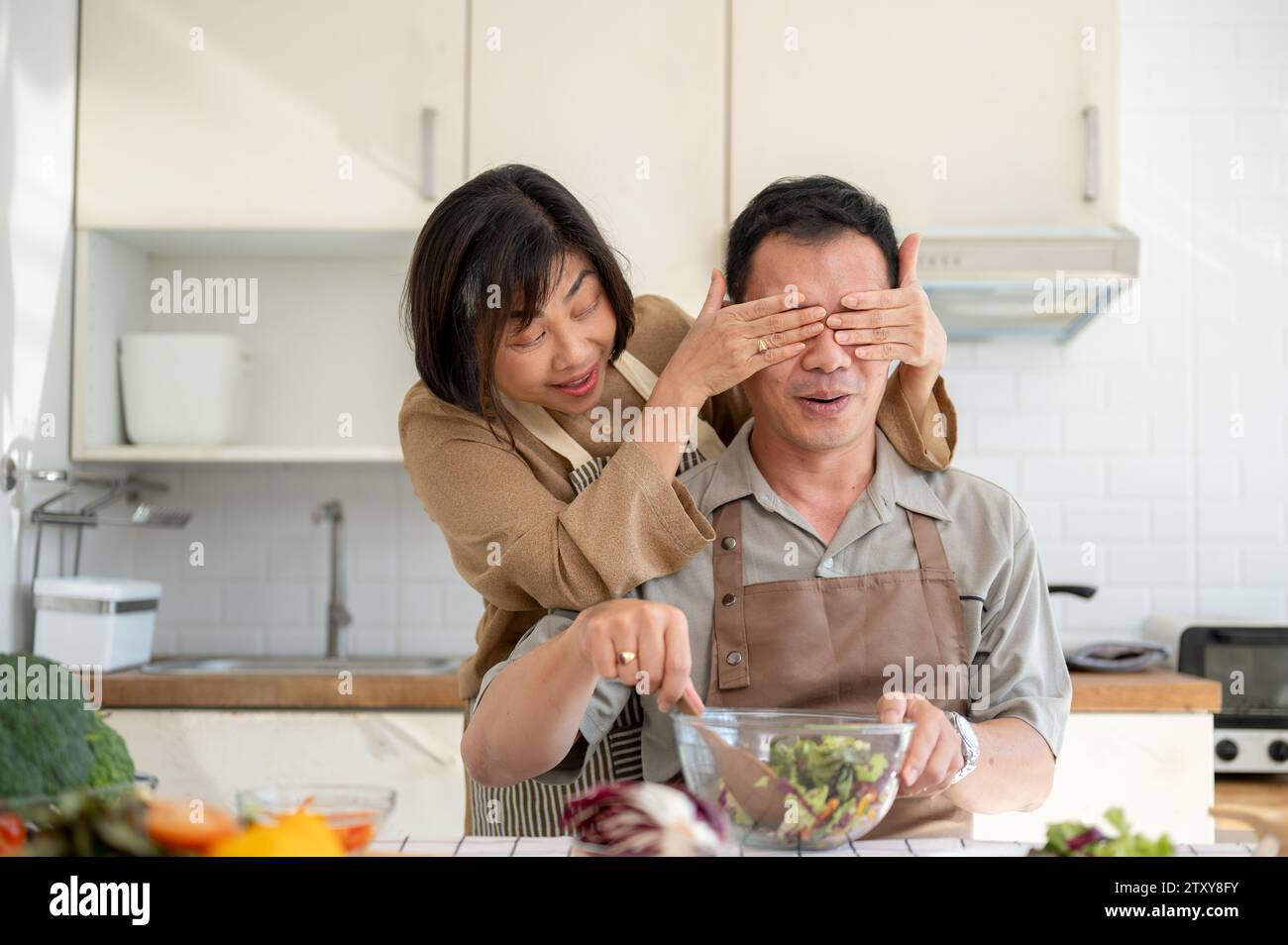 A happy, playful Asian wife is teasing her husband while he is cooking ...
