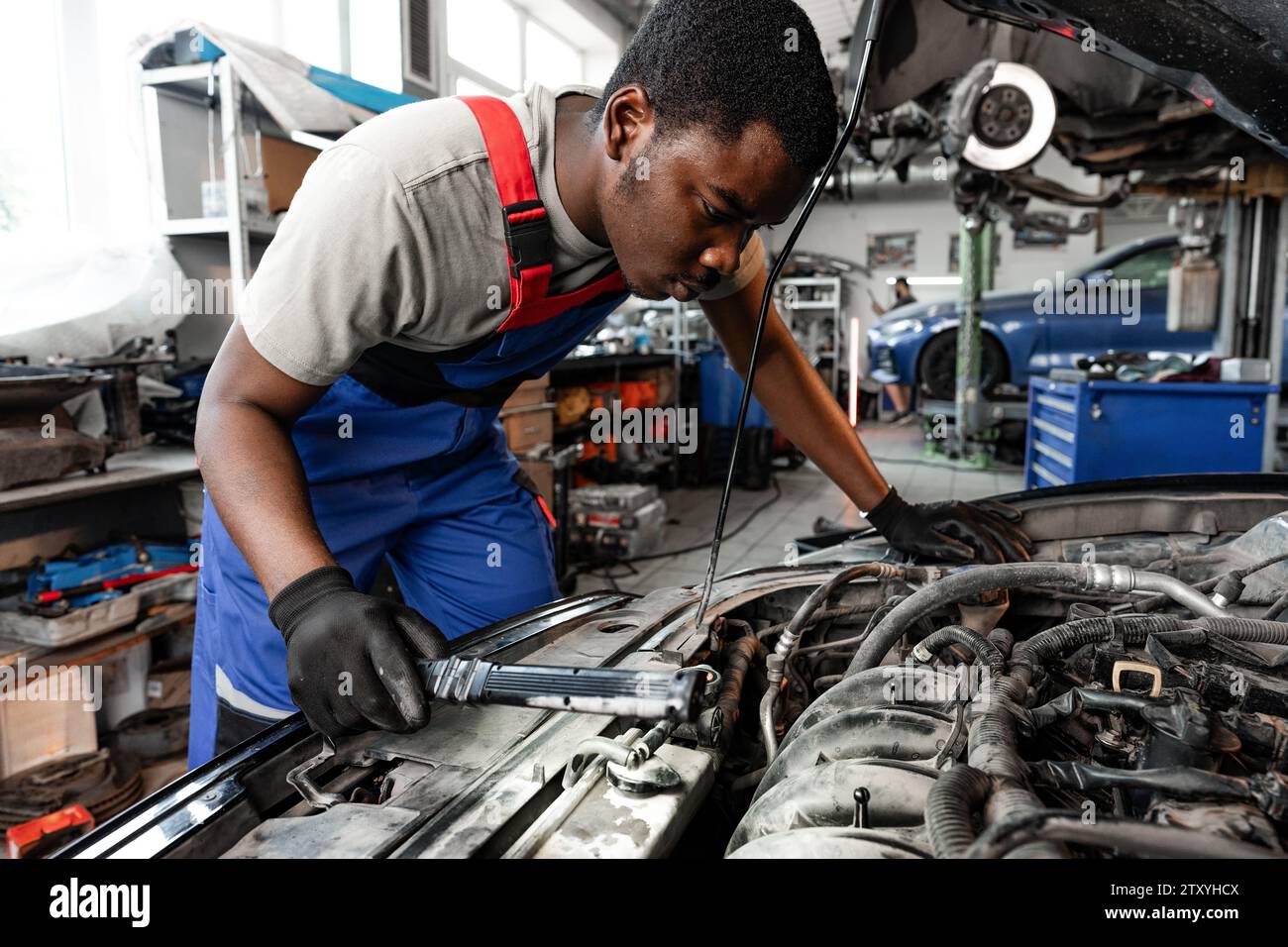 Young African auto mechanic checking car engine under the hood in auto ...