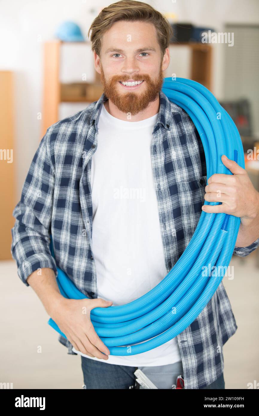 builder carrying a reel of blue pipe across his body Stock Photo - Alamy