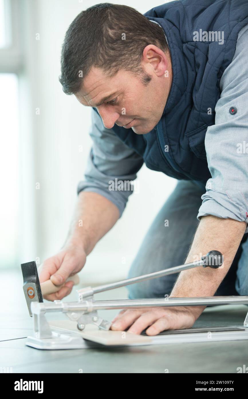 mature tiler tapping scored tile apart with hammer Stock Photo - Alamy