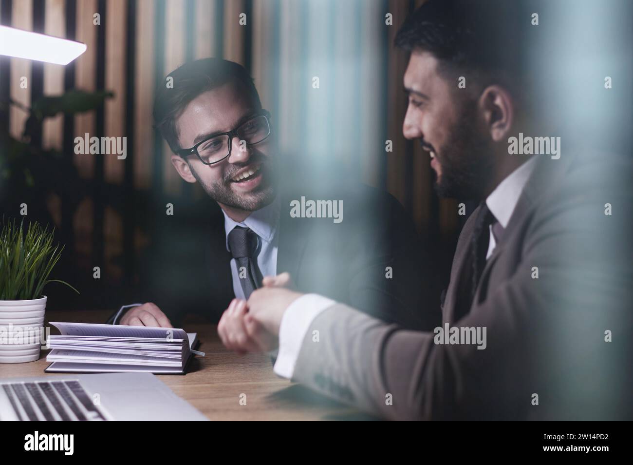 Two positive confident businessmen shaking hands over meeting table ...