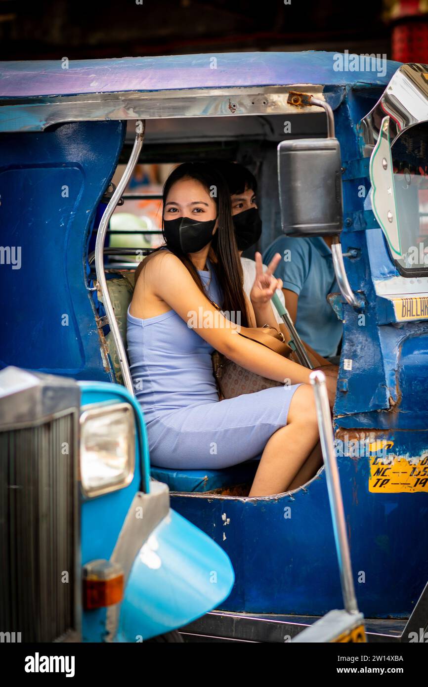 A beautiful young Filipino girl smiles and gives the V sign whilst sat ...