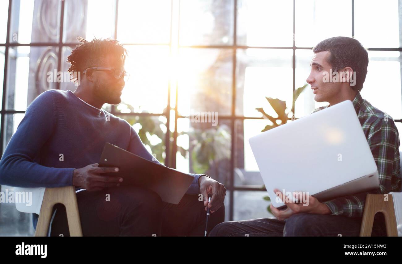 Friendly colleagues chat while sitting in the office, promising young ...