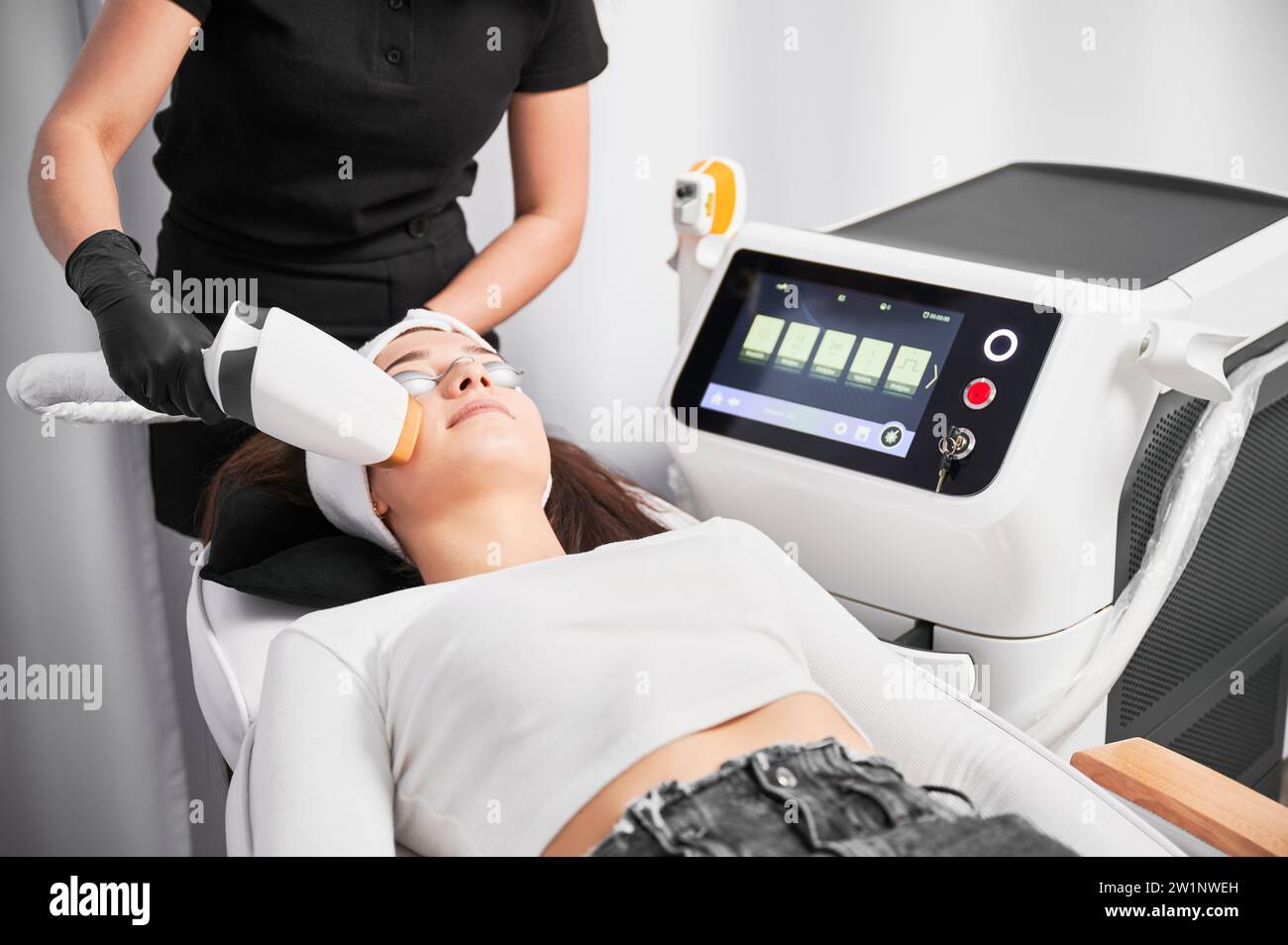 Female patient in safety glasses lying near cosmetology equipment and ...