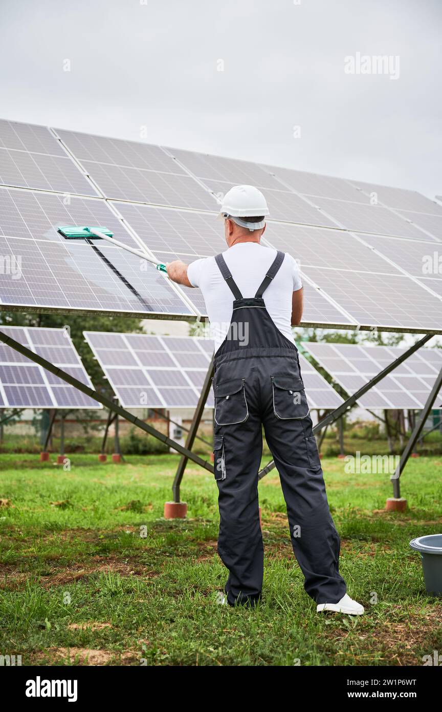 Worker in overalls and helmet cleaning solar battery by mop. Man making ...