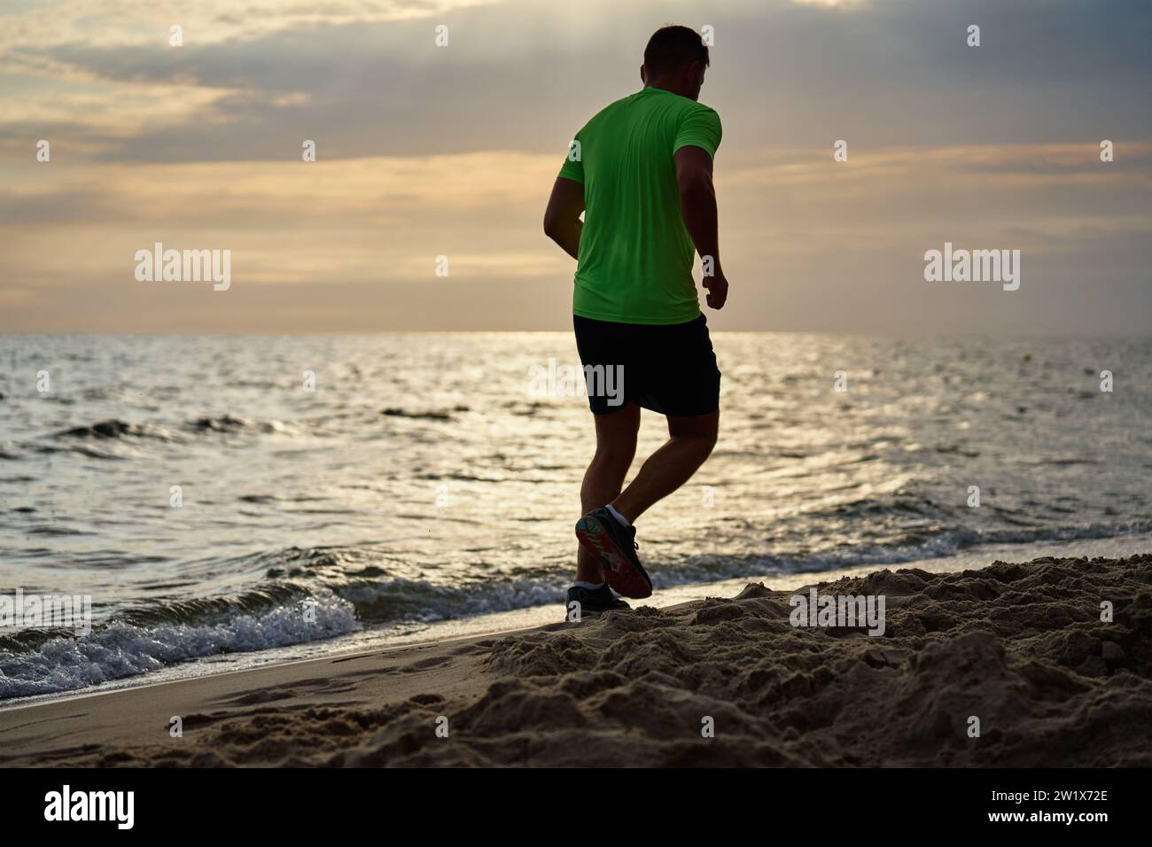 Back view of man jogging along sea beach at morning, Male athlete ...