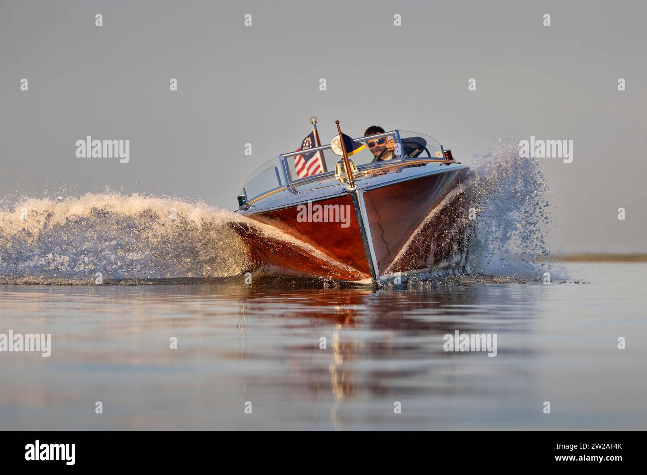 A classic, wooden speedboat approaching head-on while sharply turning ...
