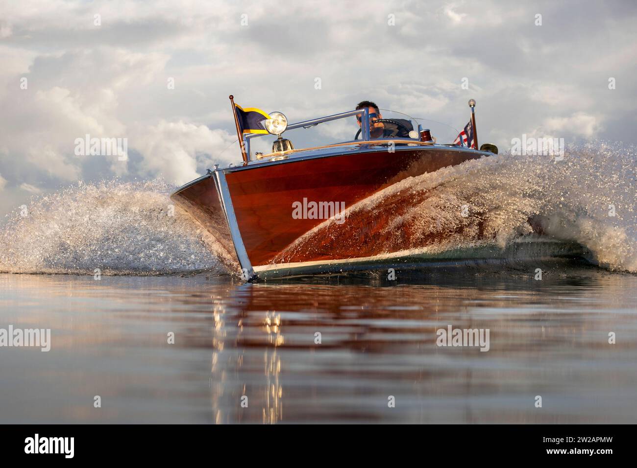 A vintage, wood speedboat sharply turning at high speed on calm water ...