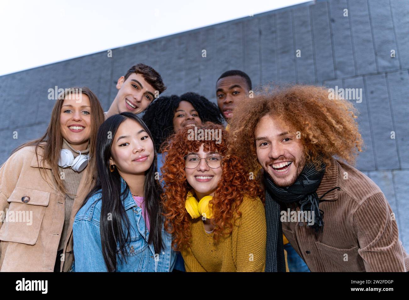 A multicultural group of seven friends huddle for a joyful photo, with ...