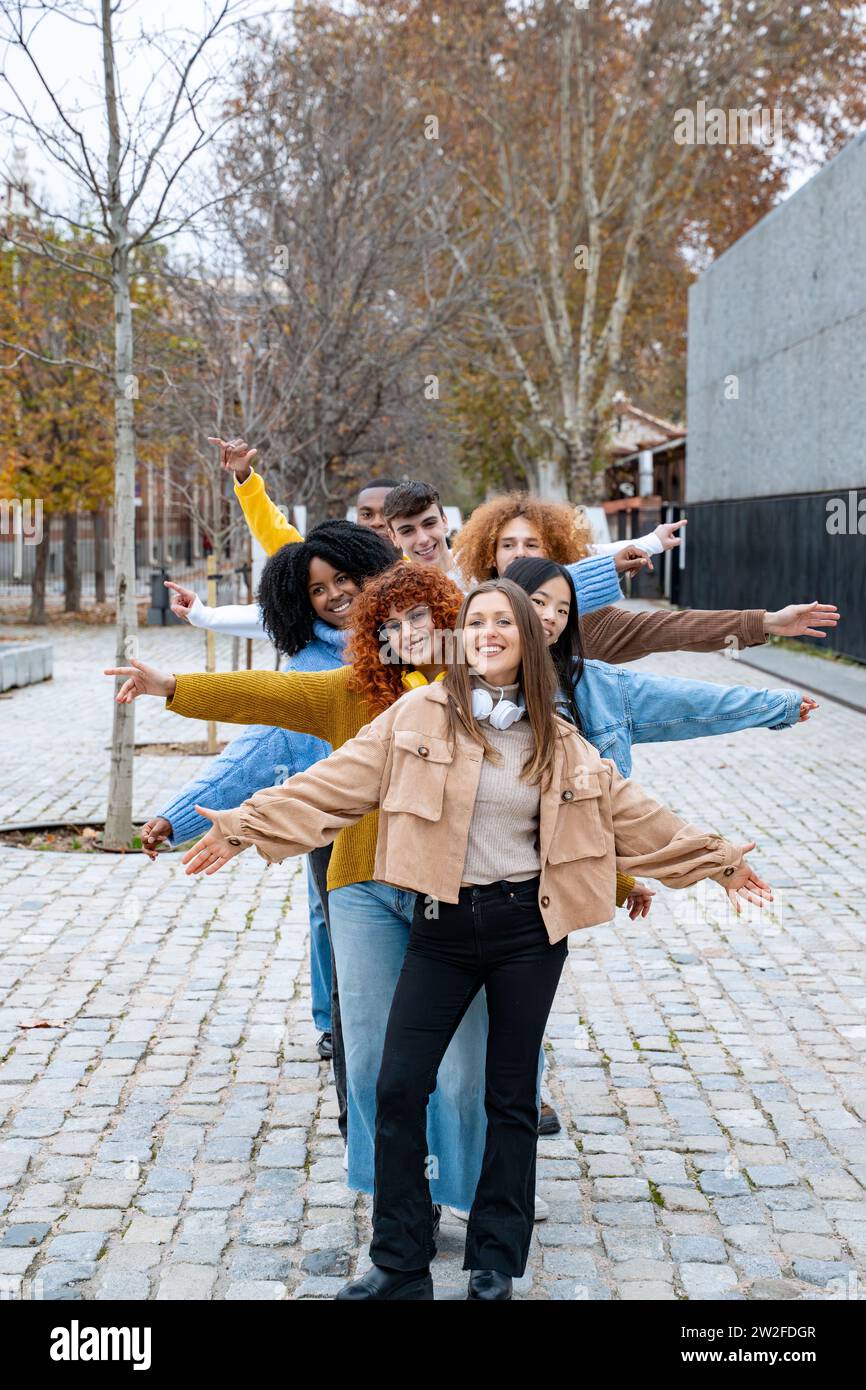 Joyful group of young friends playfully posing with arms spread wide on ...