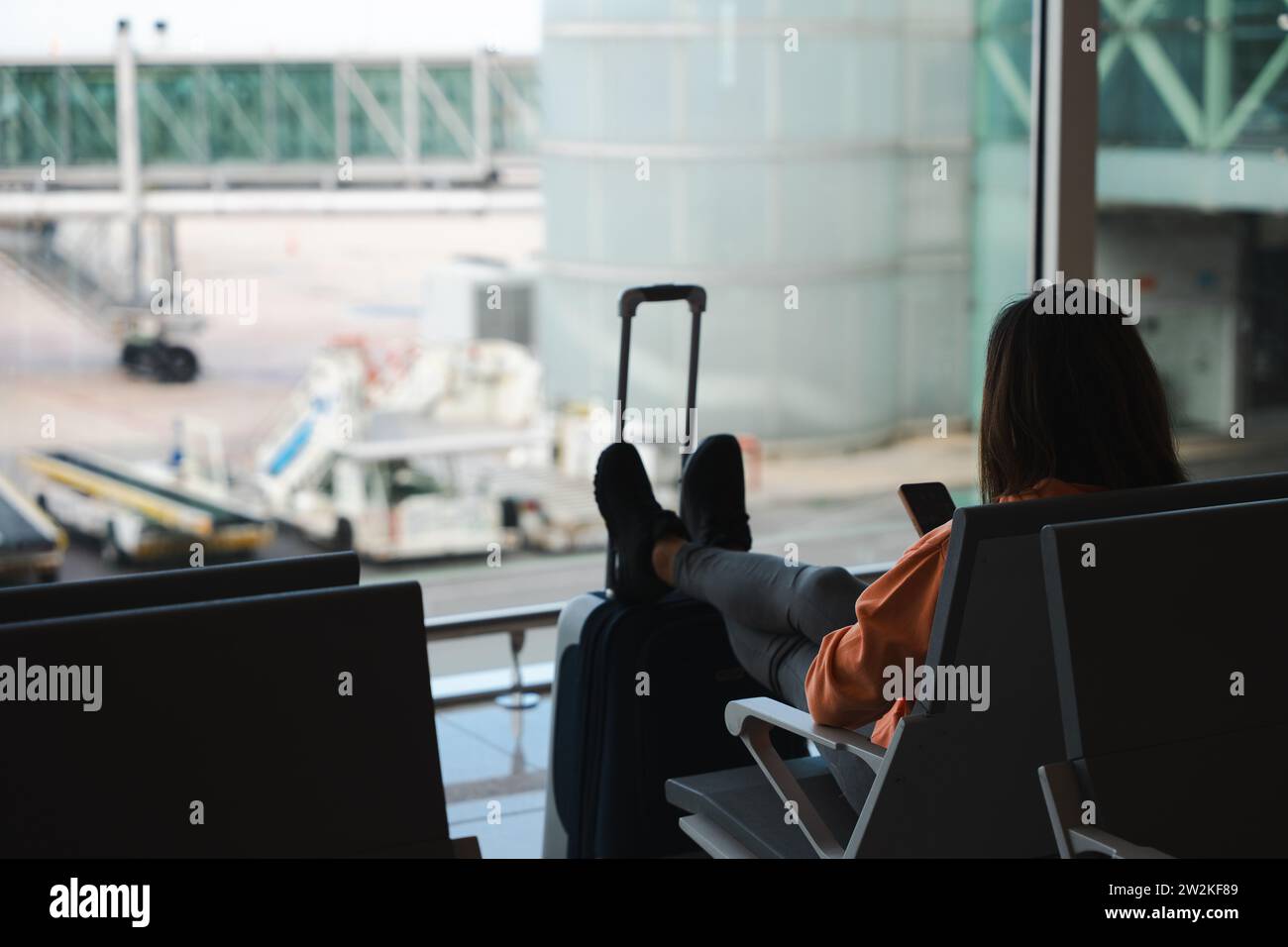 Woman checks her mobile phone while waiting for her flight at the airport Stock Photo - Alamy