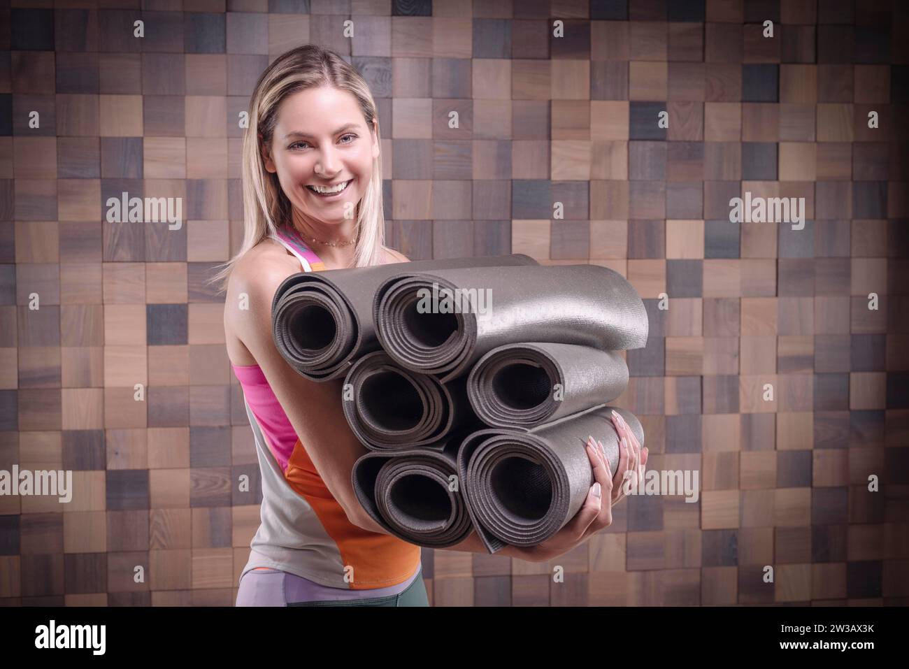 Image of a cheerful adult woman carrying a stack of rolled exercise ...