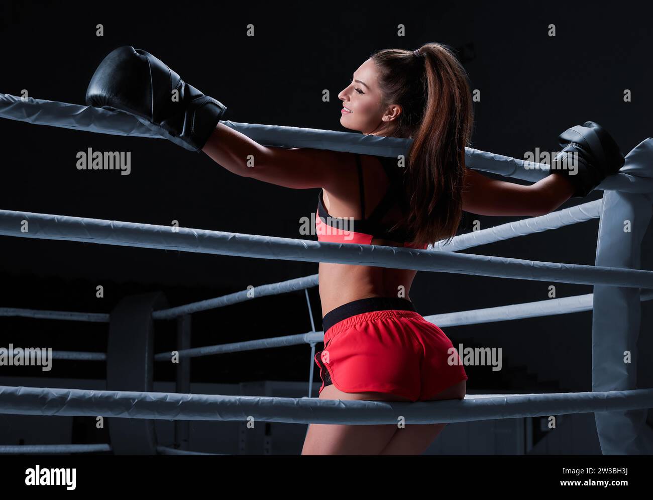 Charming woman in boxing gloves posing in the ring near the ropes ...