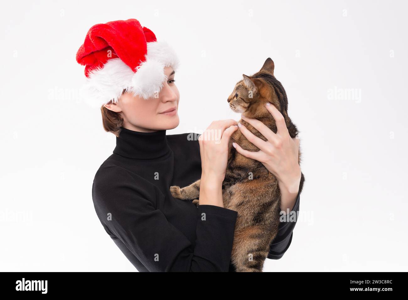 Image of a woman in a Santa Claus hat holding a cat in her arms. Light ...
