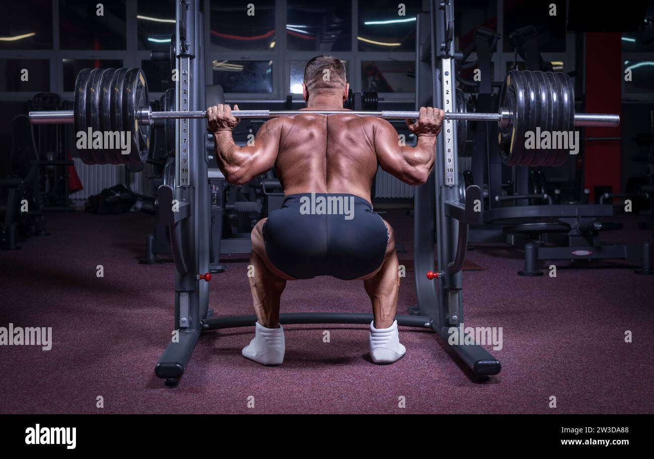 Image of a powerful athlete squatting with a barbell in a gym. Fitness ...