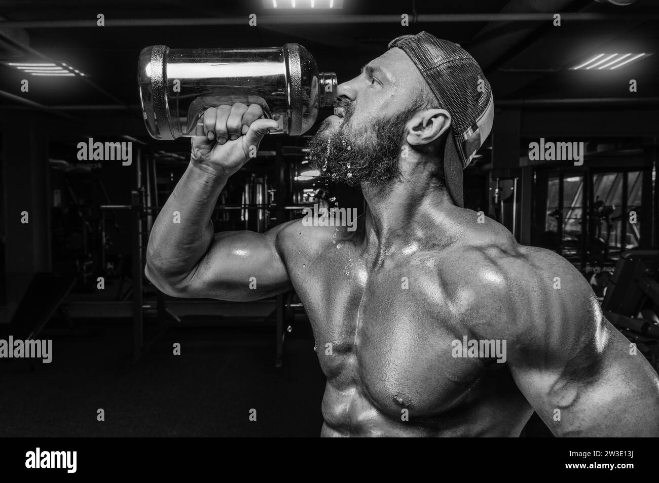 Muscular man in the gym drinks from a huge bottle. Fitness and ...