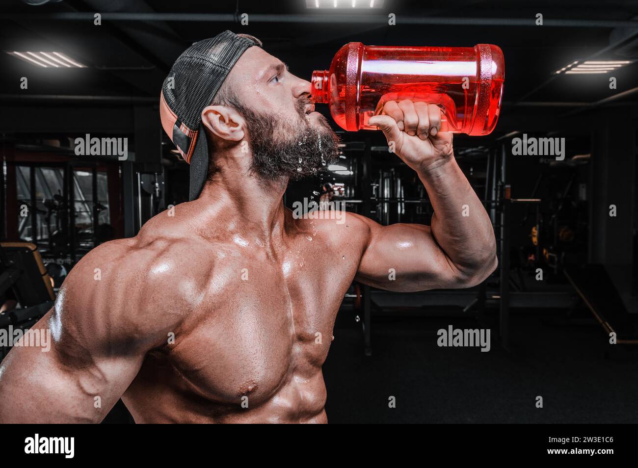 Muscular man in the gym drinks from a huge bottle. Fitness and ...