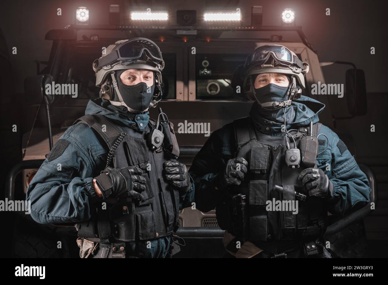 Two men in military uniforms stand in a hangar with a truck in the ...