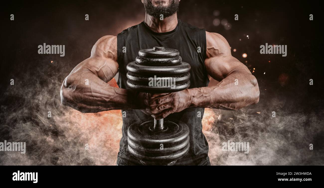 Muscular man posing with a dumbbell on a background of fire and smoke ...