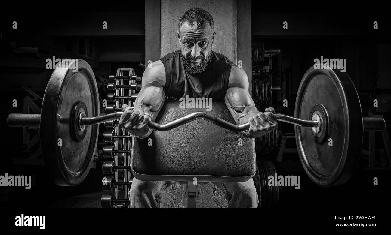 Muscular man sits on a bench with a barbell in the gym. Bicep pumping ...