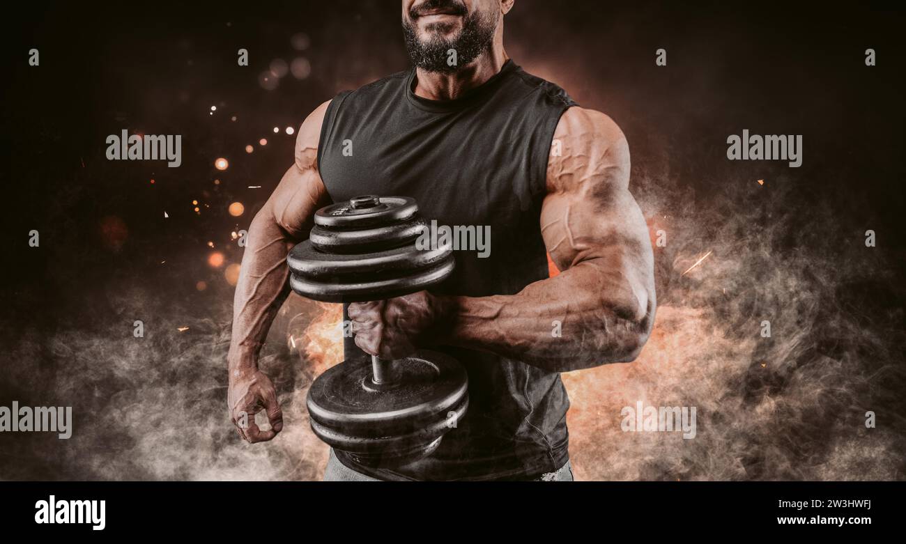 Muscular man posing with a dumbbell on a background of fire and smoke ...