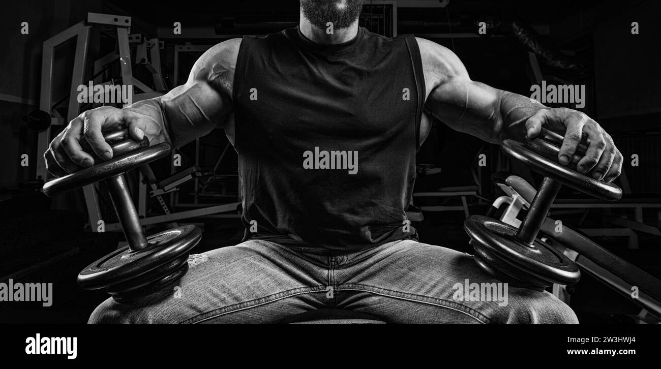 Muscular man sits on a bench with dumbbells in the gym. Fitness and ...