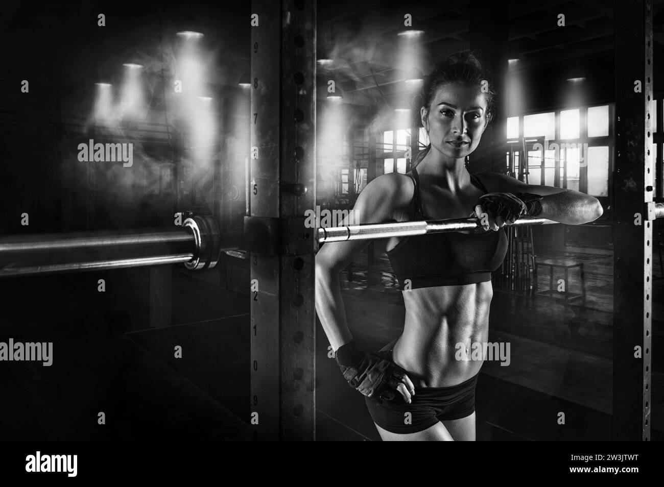 Portrait of a muscular woman near a power rack with a barbell. A dark ...