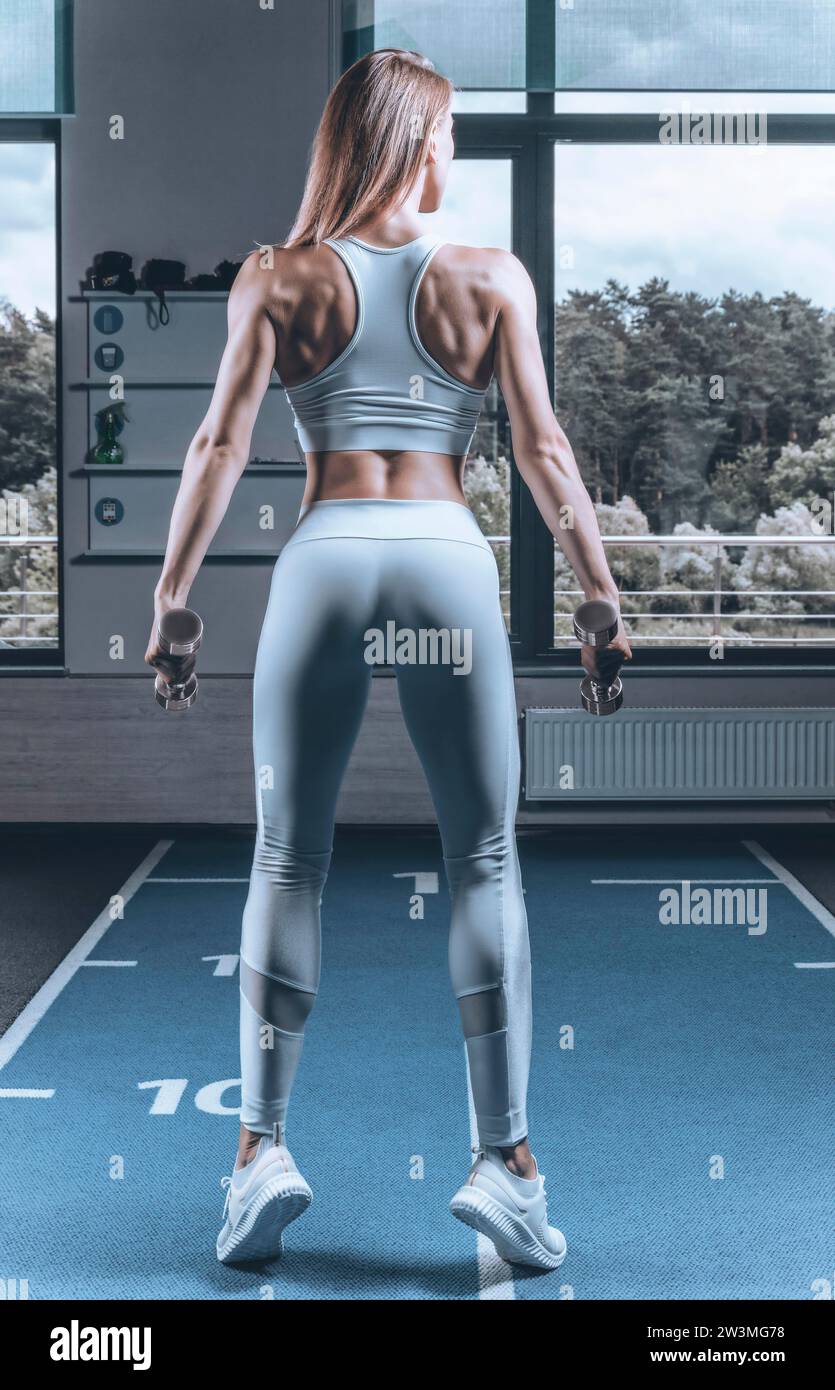 Adorable girl posing in the gym with dumbbells. Back view. The concept ...