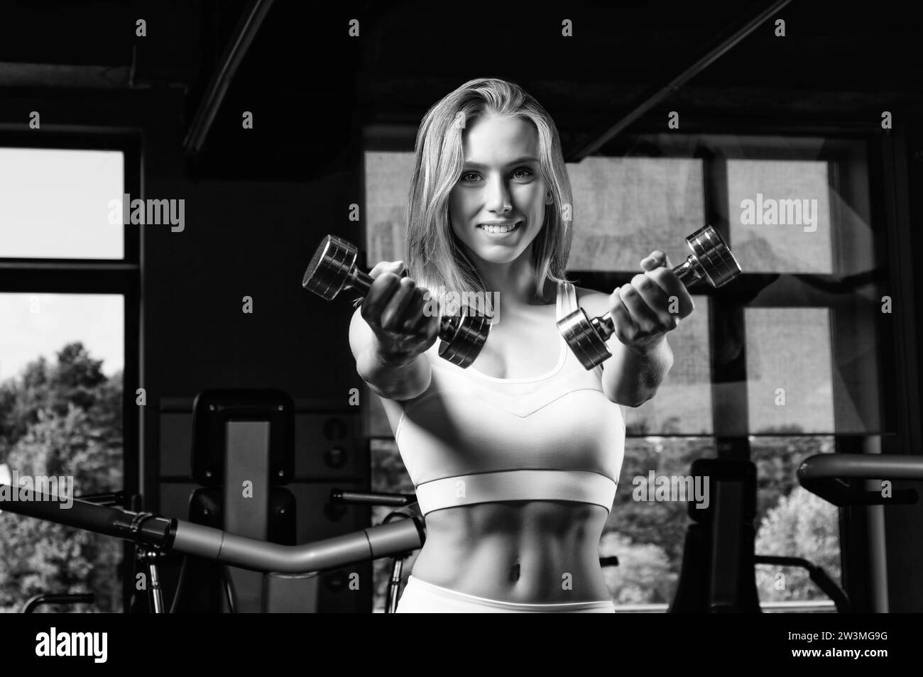 Charming young athlete is training in the gym. She stretches the ...