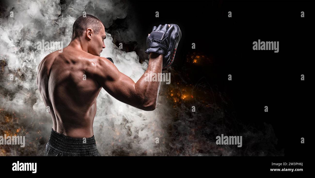 Muscular fighter posing with boxing paws against a background of smoke ...