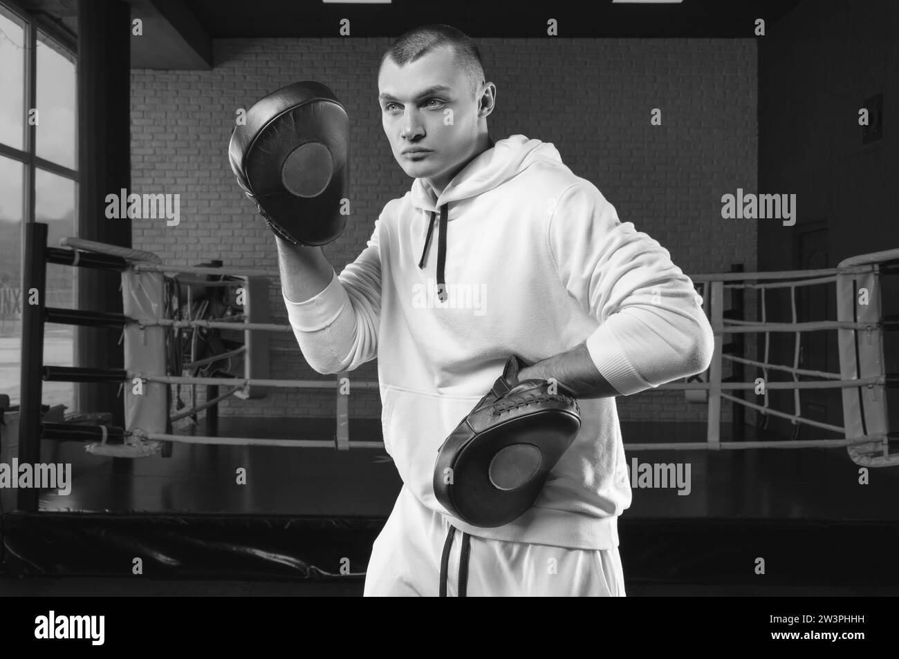 Male trainer in the gym against the background of the ring holds boxing ...