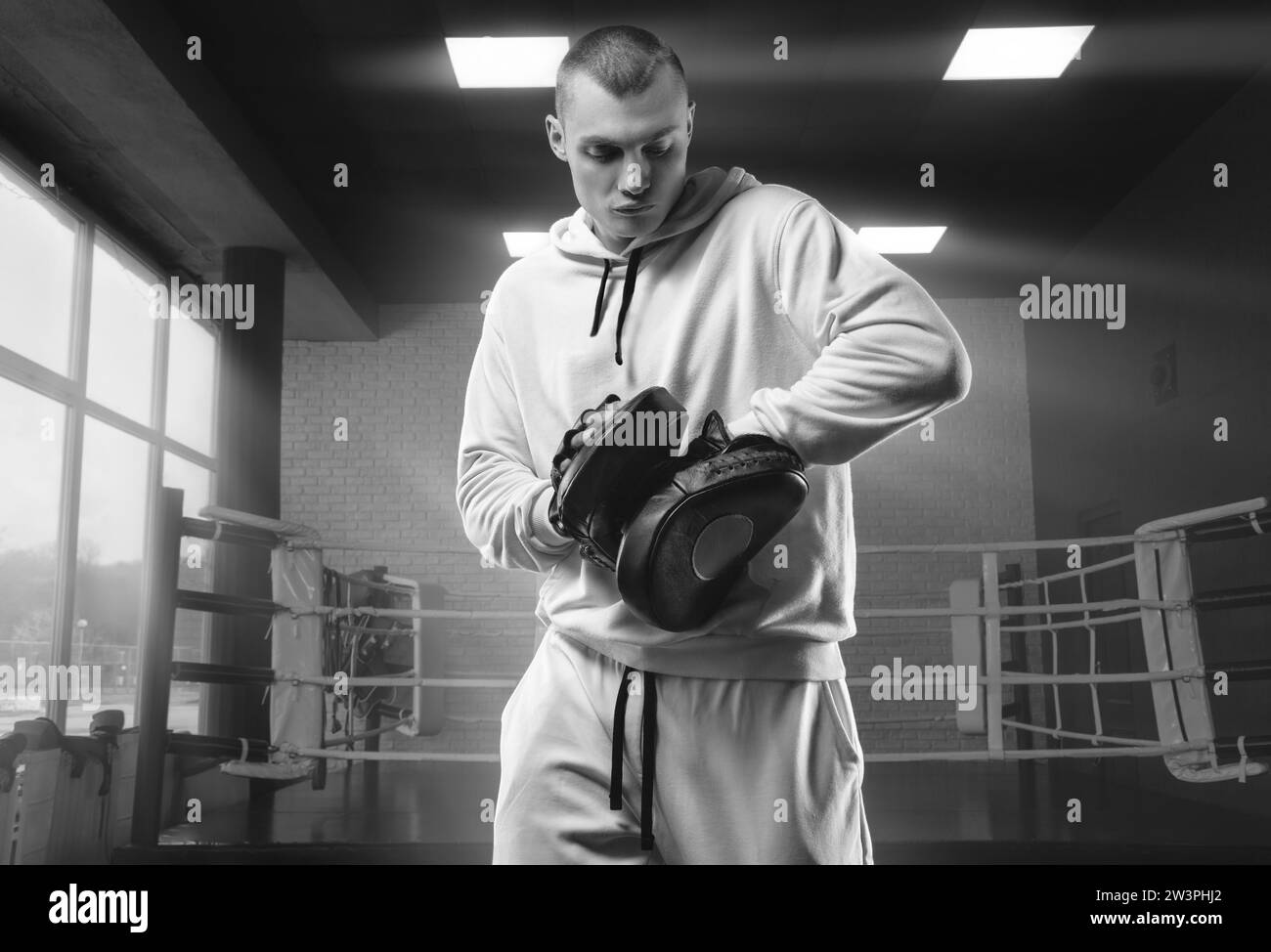 Male trainer in the gym against the background of the ring holds boxing ...
