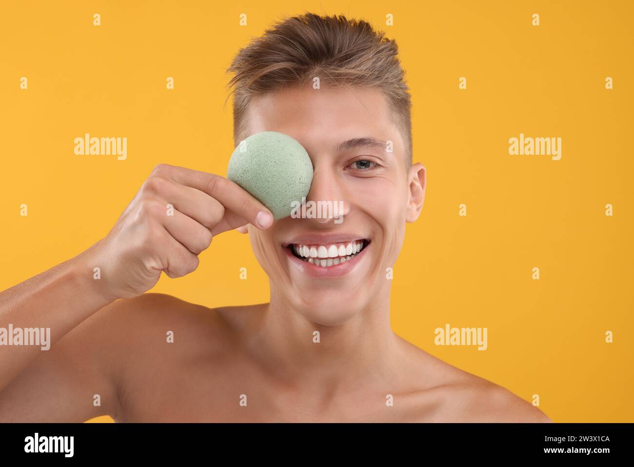 Happy young man holding face sponge on orange background Stock Photo ...
