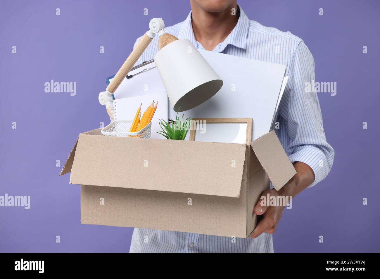 Unemployed young man with box of personal office belongings on purple ...