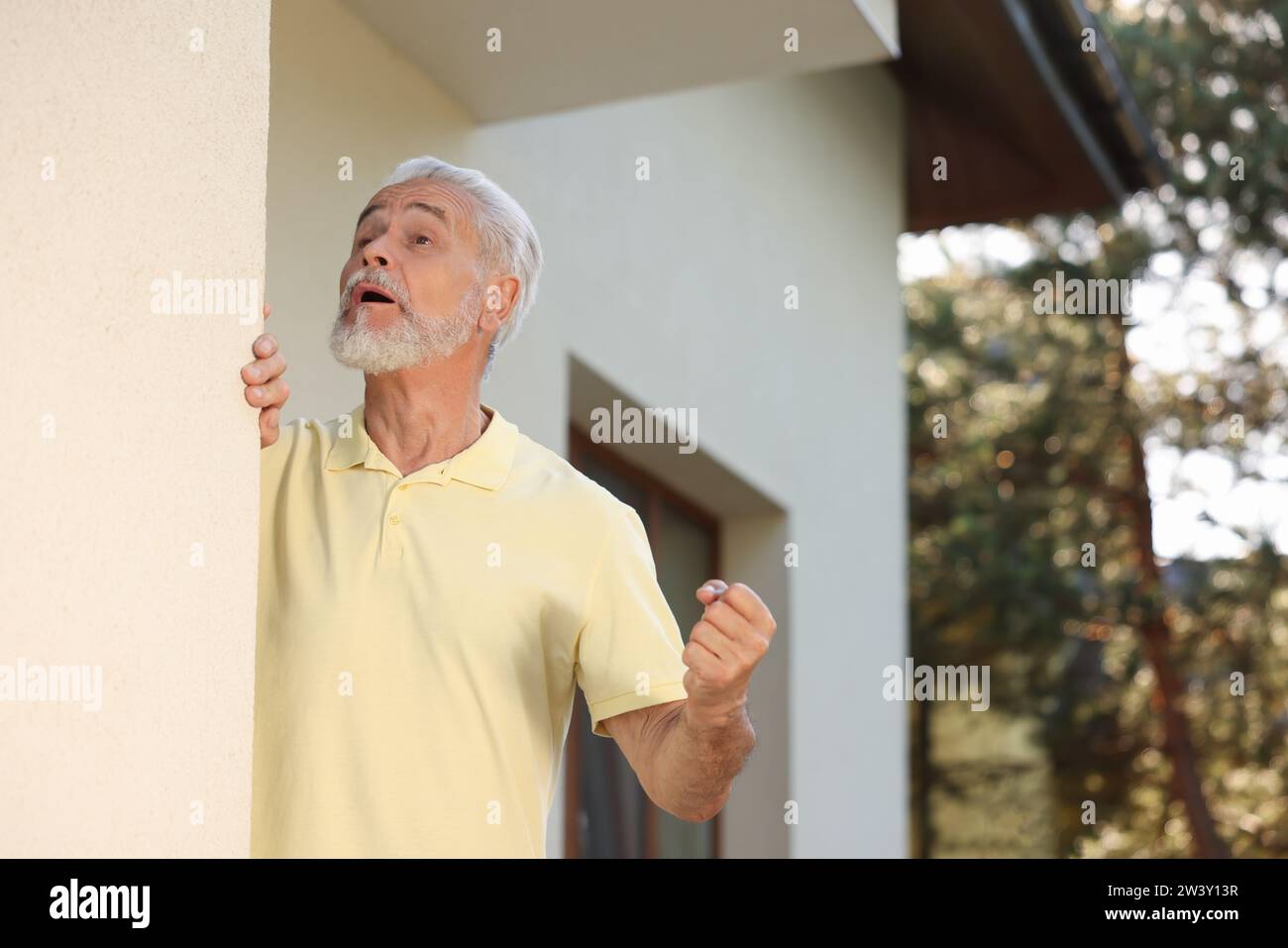 Angry senior man showing fist near house, space for text. Annoying ...