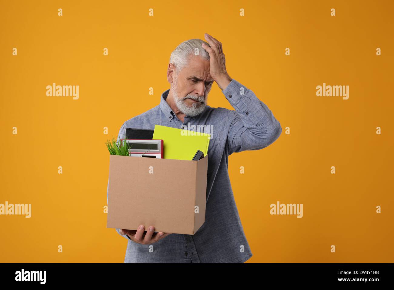 Unemployed senior man with box of personal office belongings on orange ...