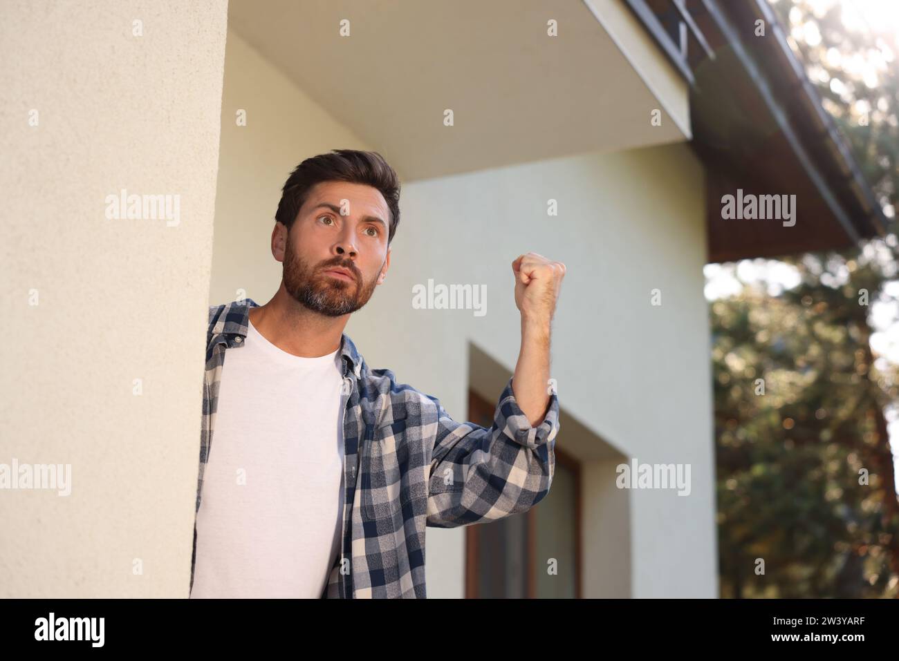 Angry man showing fist near house, low angle view. Annoying neighbour ...