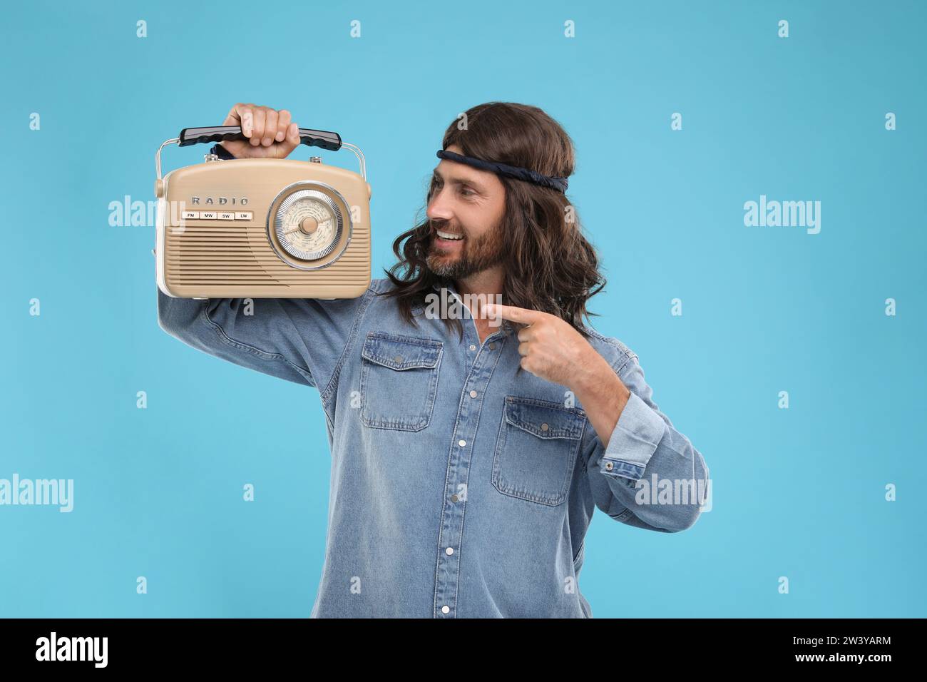 Stylish hippie man pointing at retro radio receiver on light blue ...