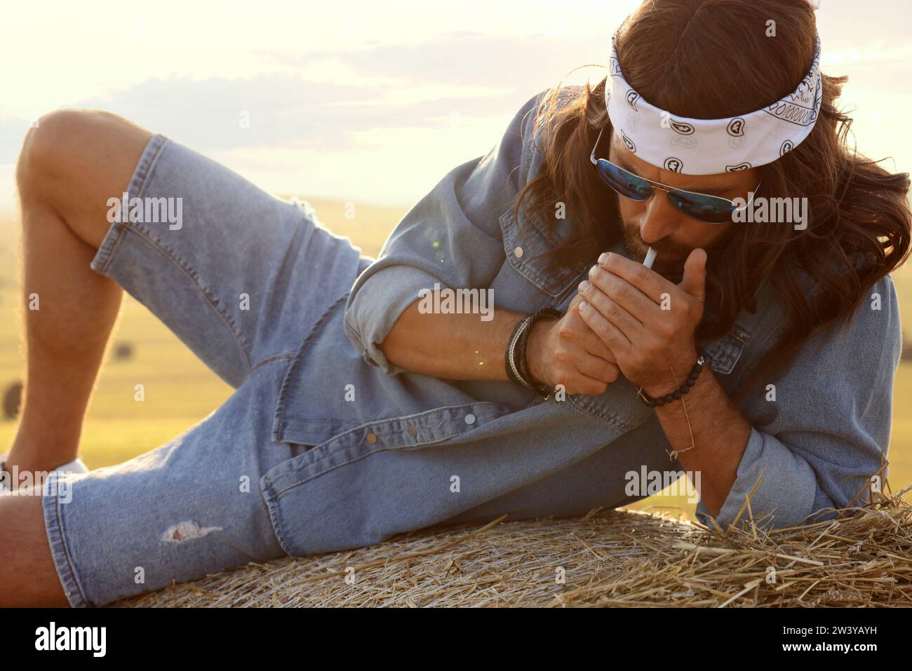 Hippie man smoking joint on hay bale in field Stock Photo - Alamy