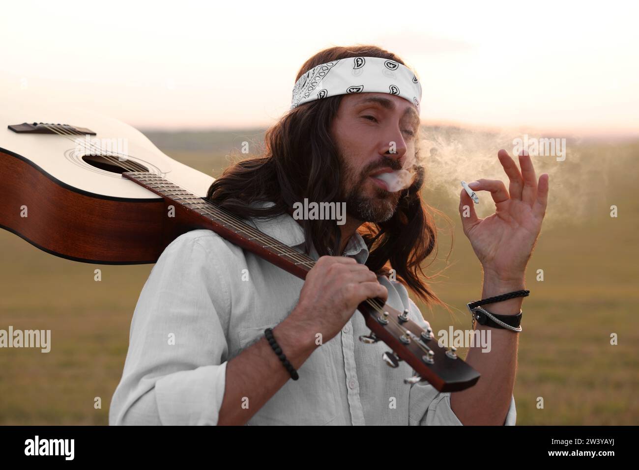 Stylish hippie man with guitar smoking joint in field Stock Photo - Alamy
