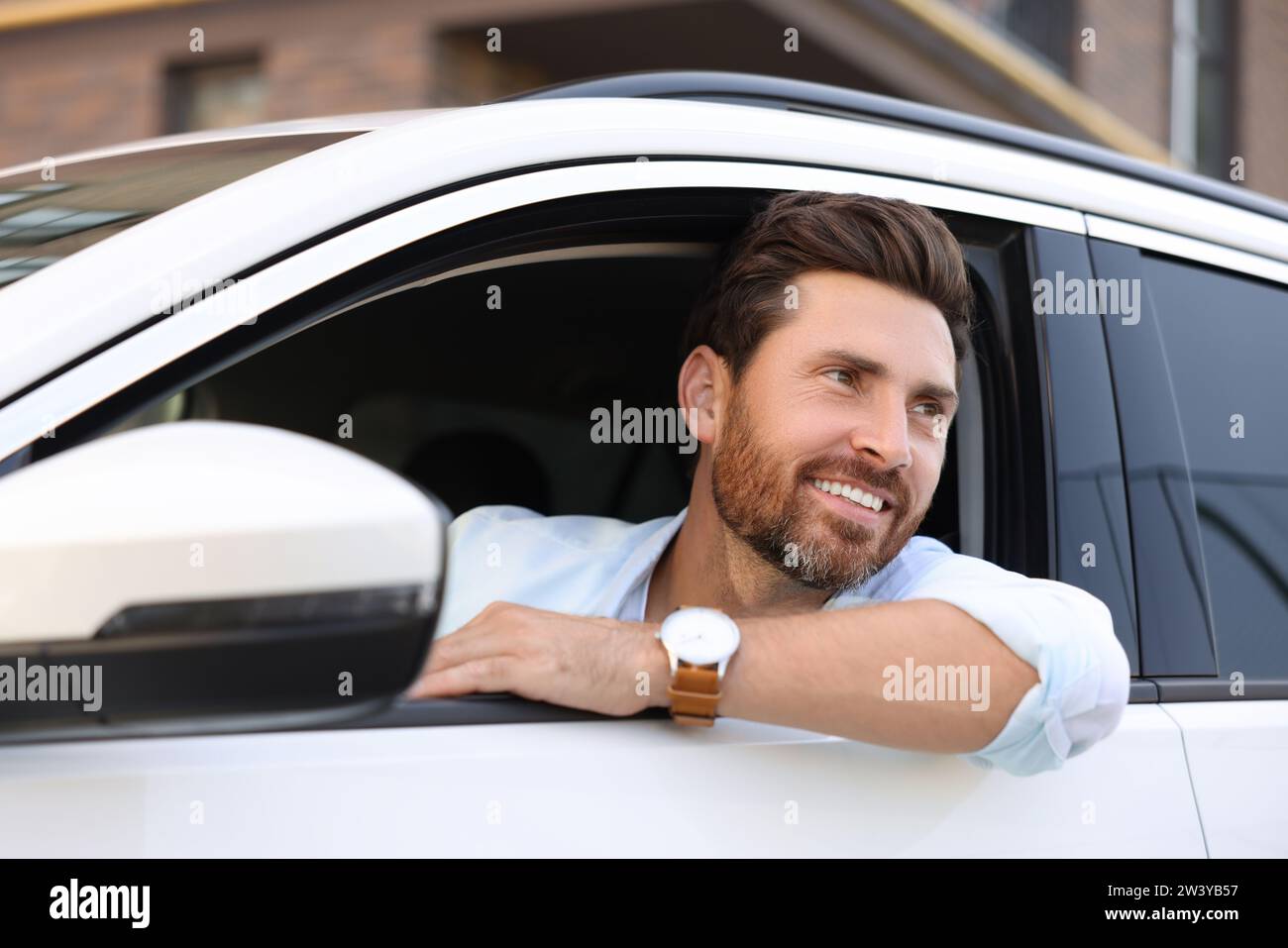 Happy bearded man looking out of car window on city street, view from ...