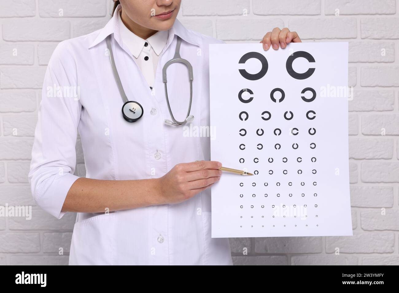 Ophthalmologist pointing at vision test chart near white brick wall ...