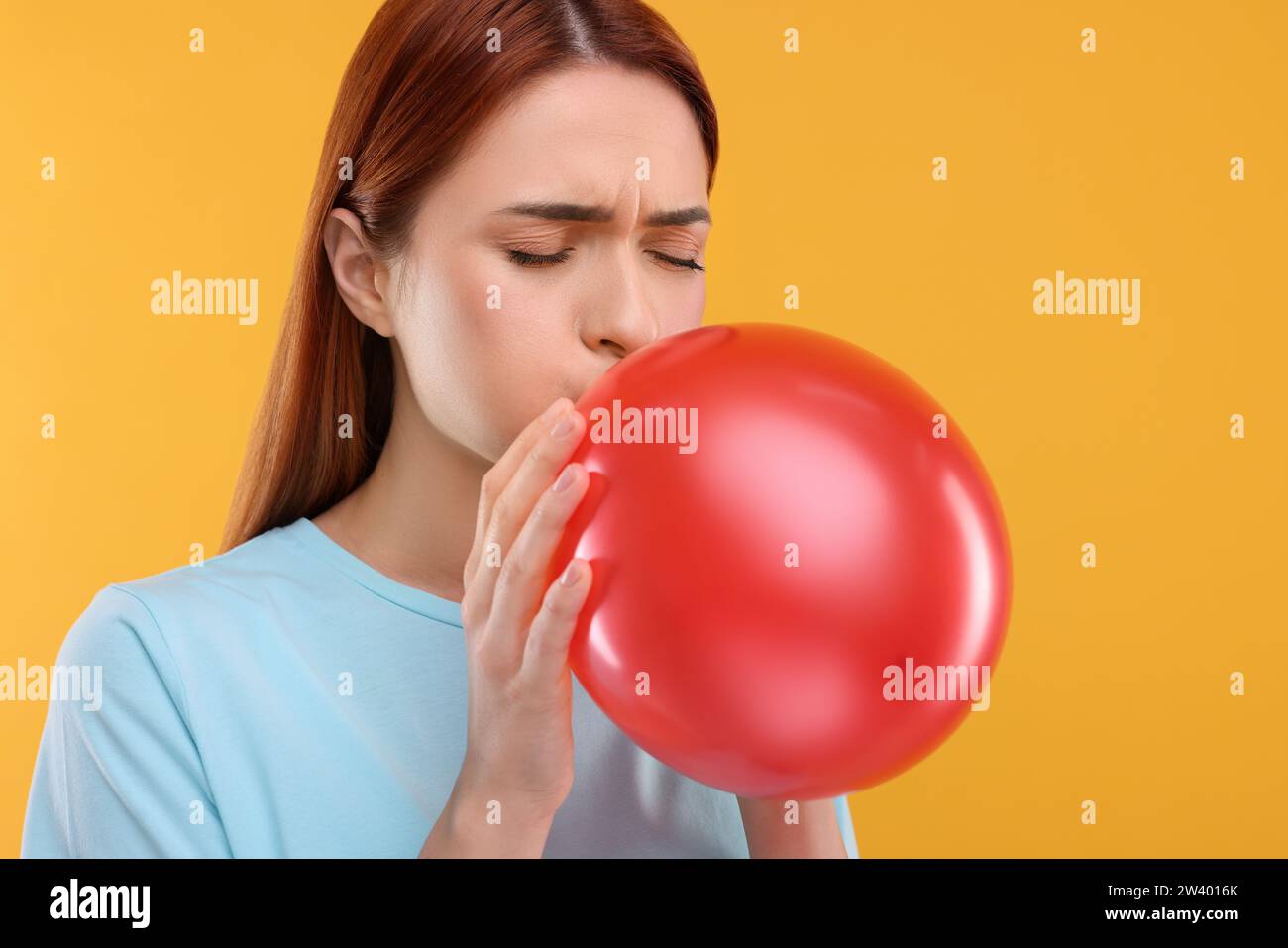 Woman inflating red balloon on orange background Stock Photo - Alamy