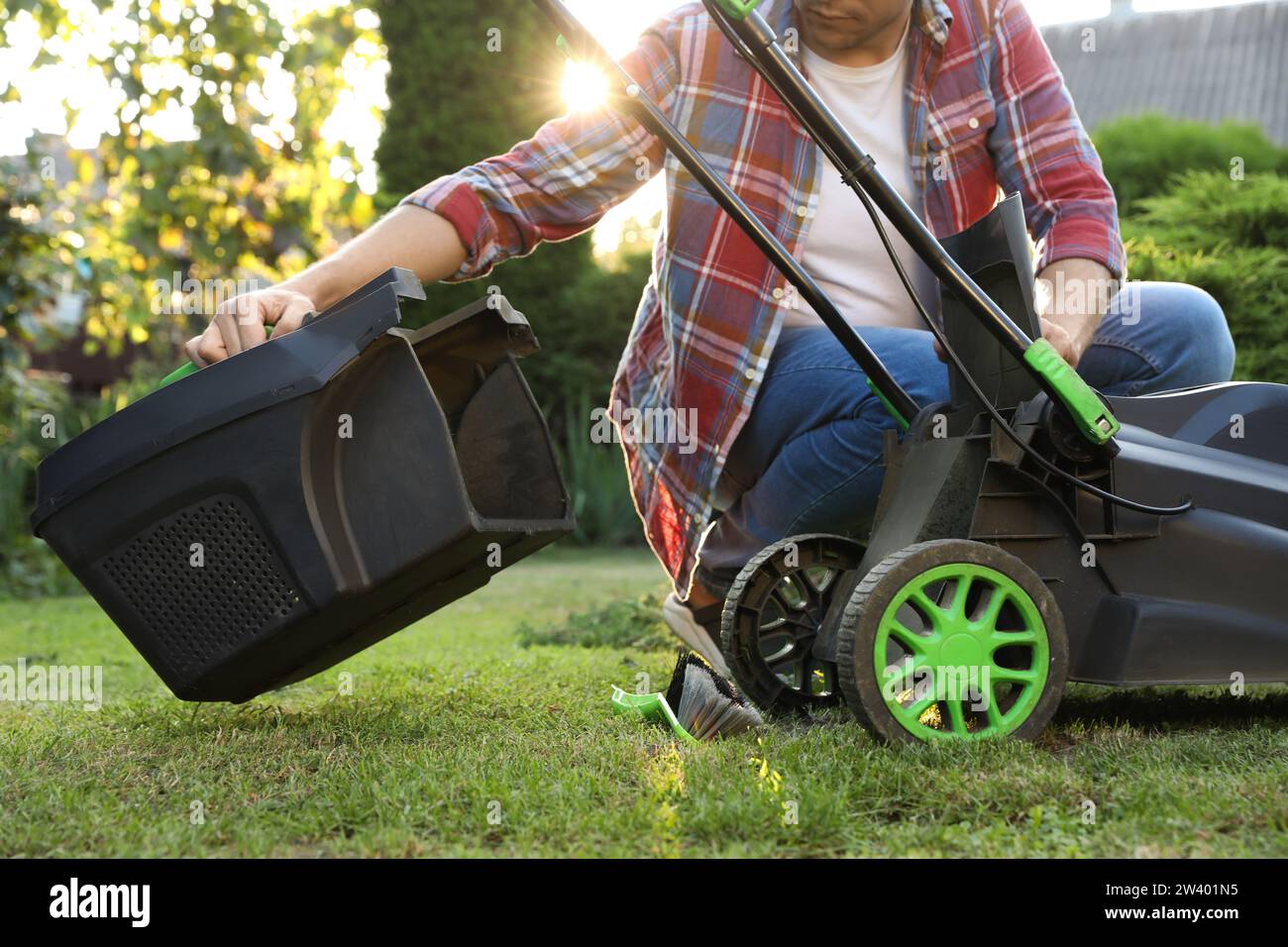Cleaning lawn mower. Man detaching grass catcher from device in garden ...